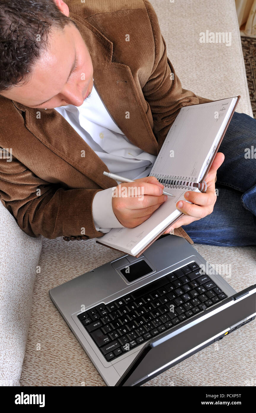 Businessman writing while sitting on the couch on note Stock Photo - Alamy