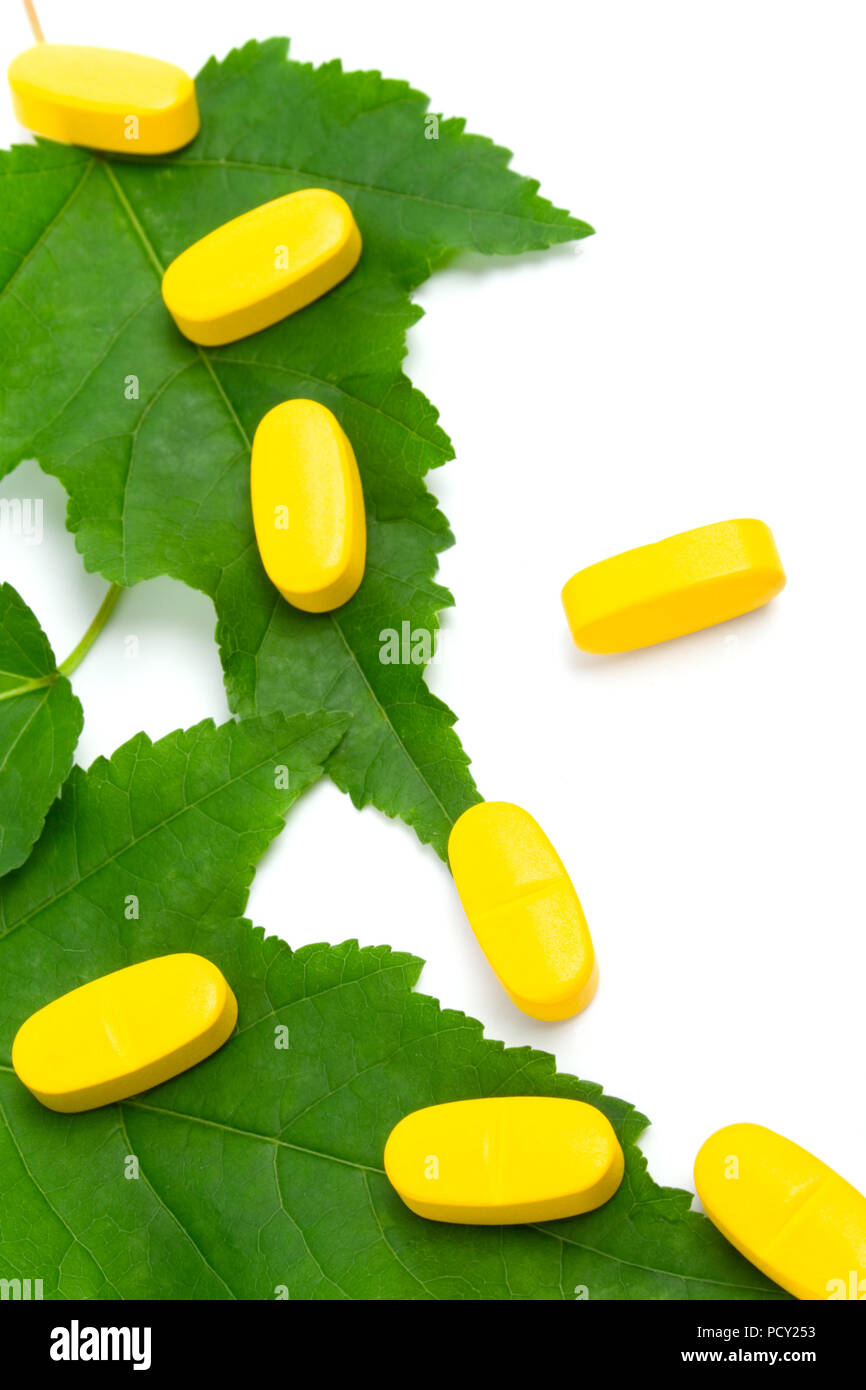 yellow vitamin pills over green leaves on white background Stock Photo ...