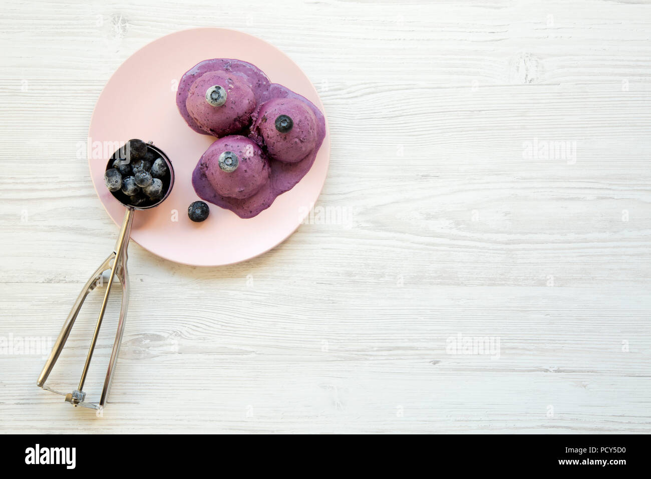Blueberry ice cream balls with icecream scoop on a pink plate over ...