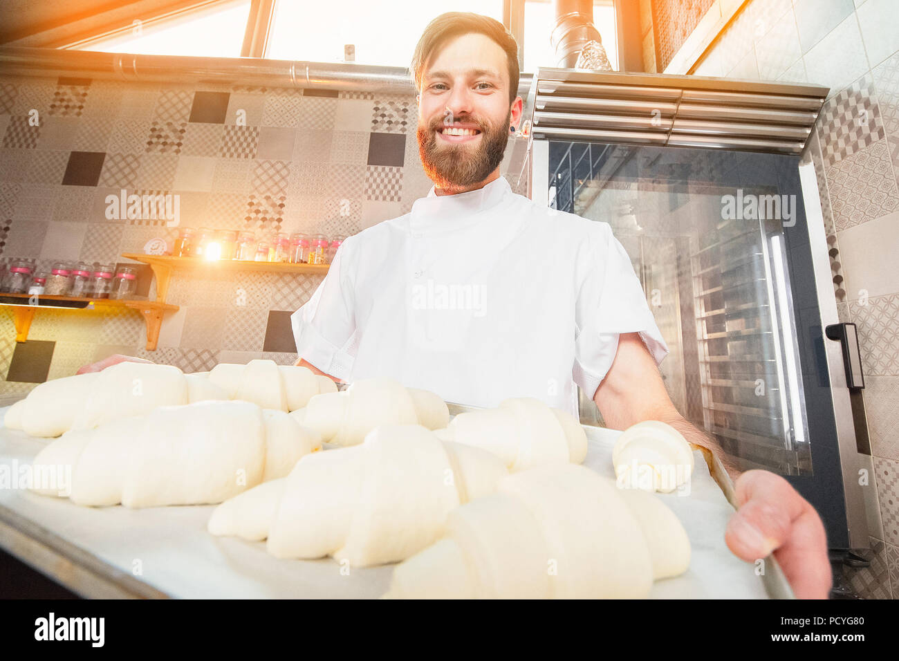 A young handsome baker is holding raw croissants of white dough in the ...