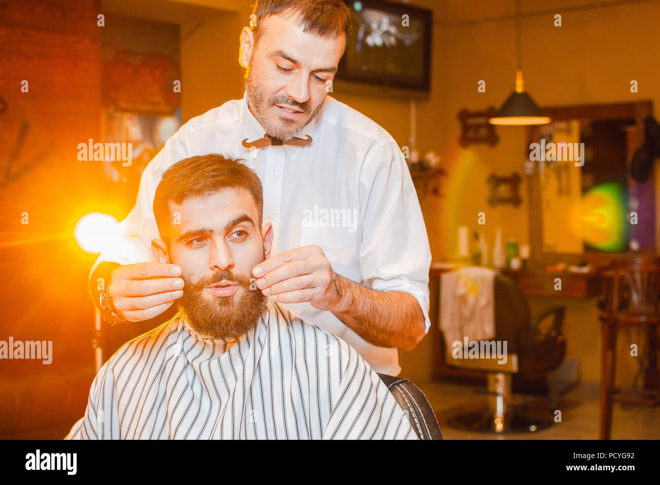 Barber makes a styling mustache for a young handsome guy in a male ...