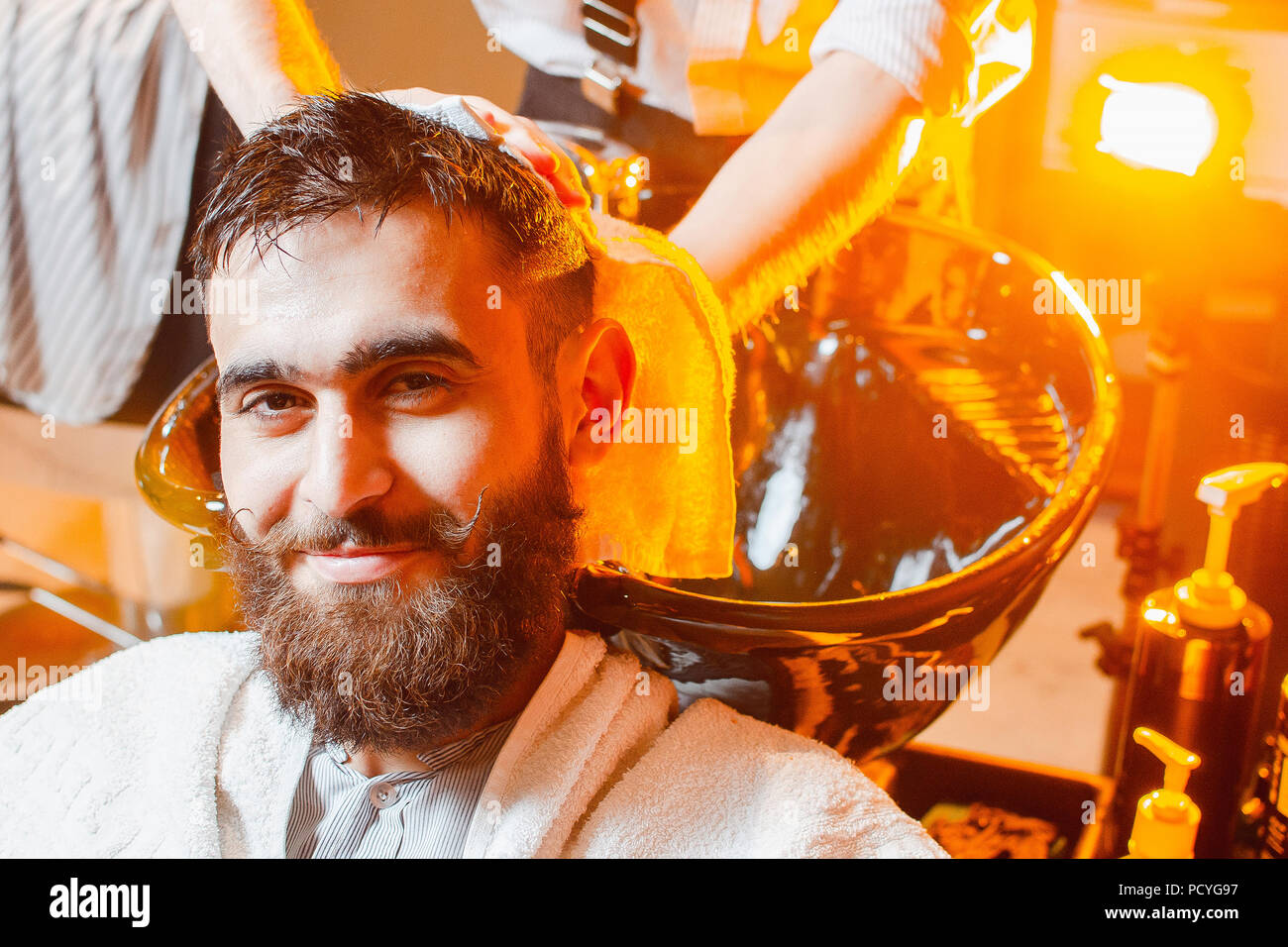Barber washes the head of a young handsome guy with a beard and ...