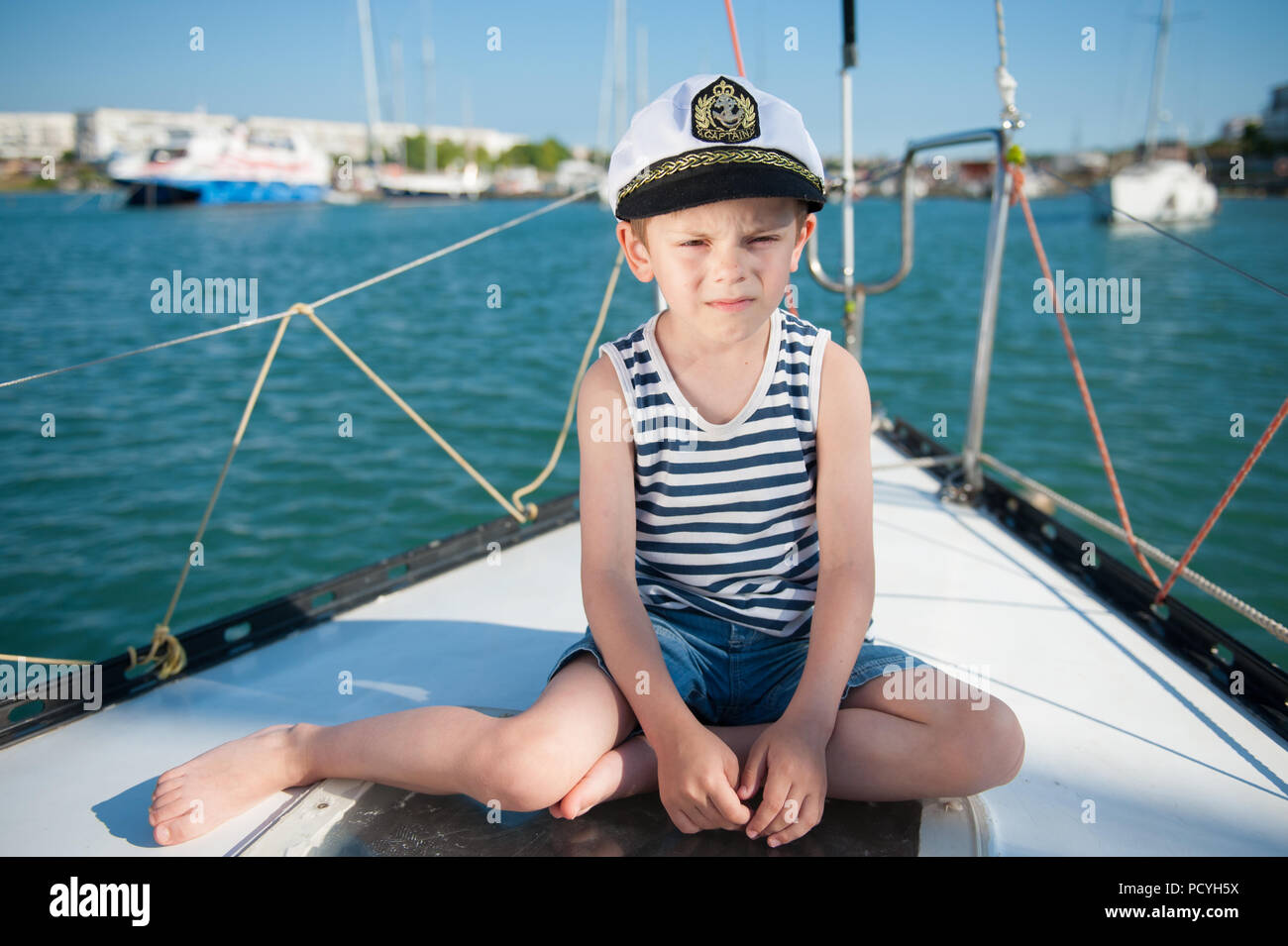 serious caucasian kid in captain hat sitting on luxury yacht board in ...