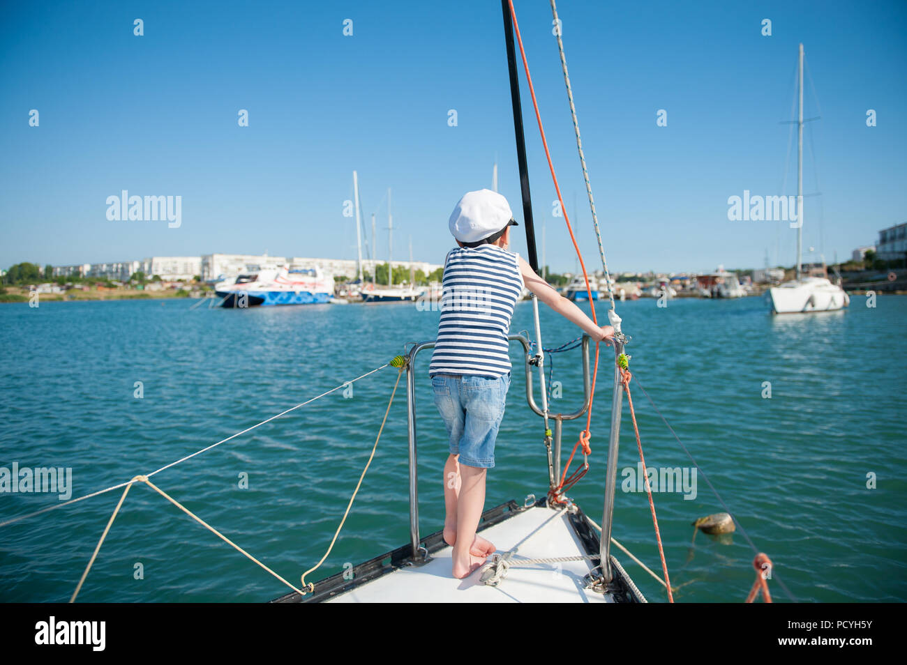 healthy small boy in captain hat standing on luxury yacht board in sea ...