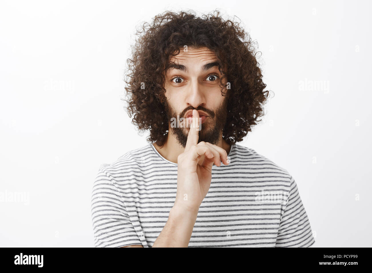 Portrait of intigued attractive curly-haired guy with beard, standing ...