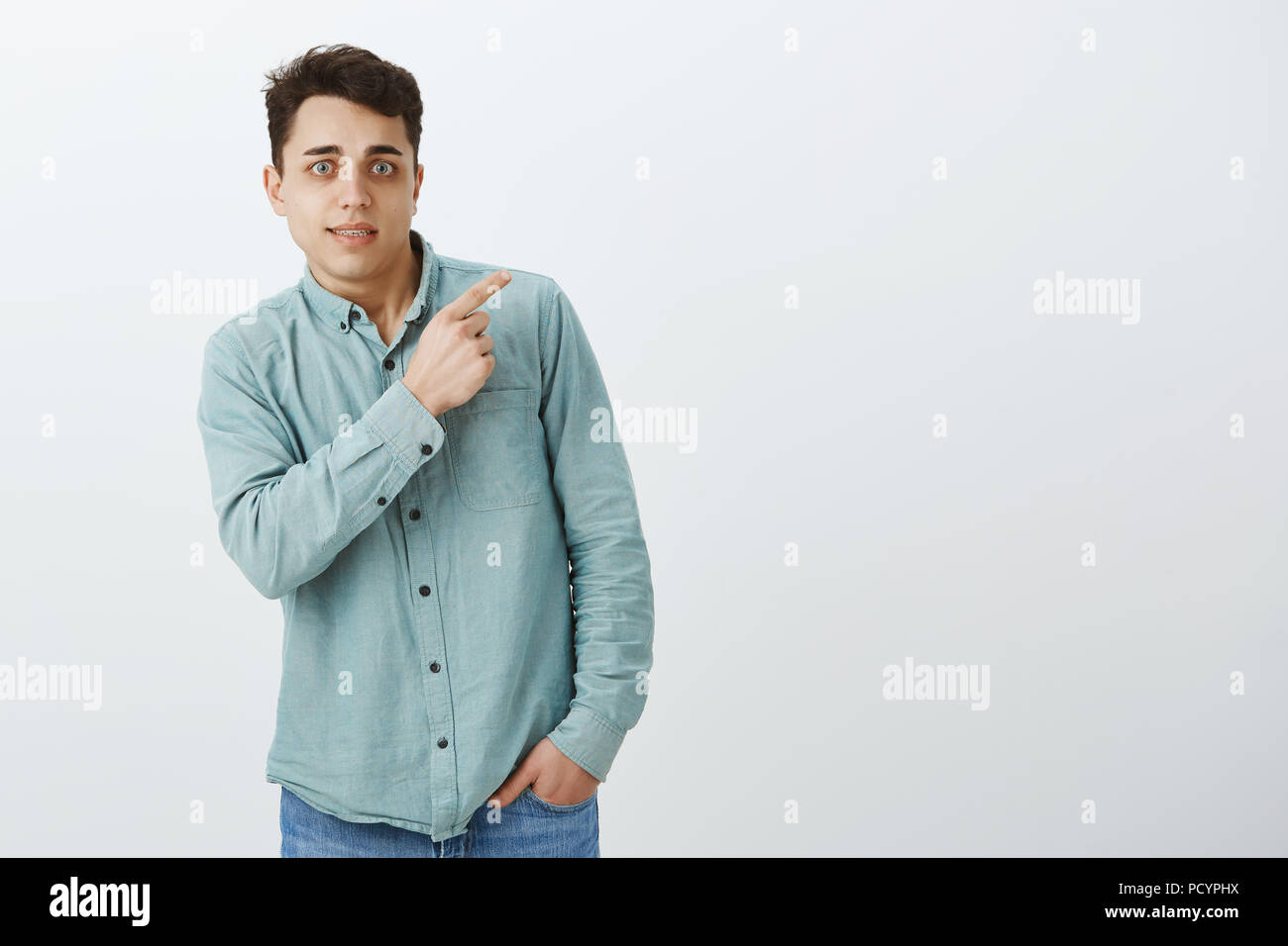 Indoor shot of boyfriend in casual clothes, tilting left and pointing ...