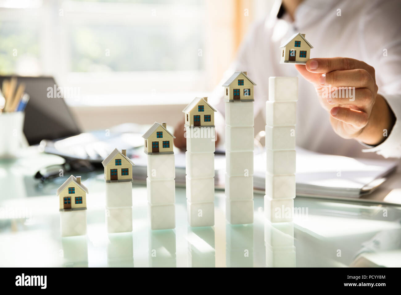 Increasing house models arranged in a row on reflective desk Stock ...