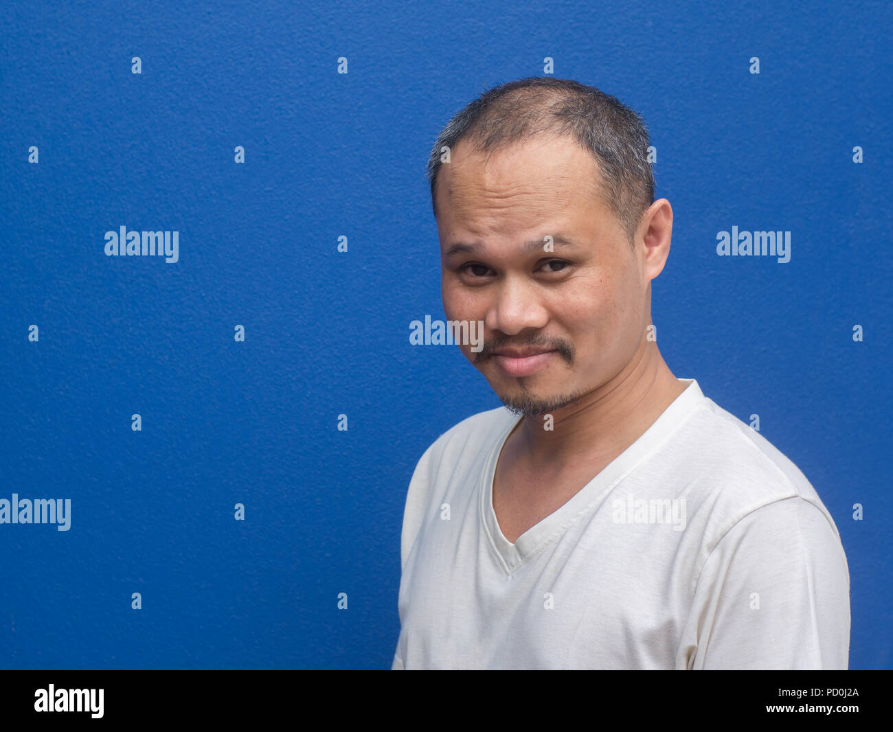 Asian man smilingly wearing white shirt against blue cement wall ...