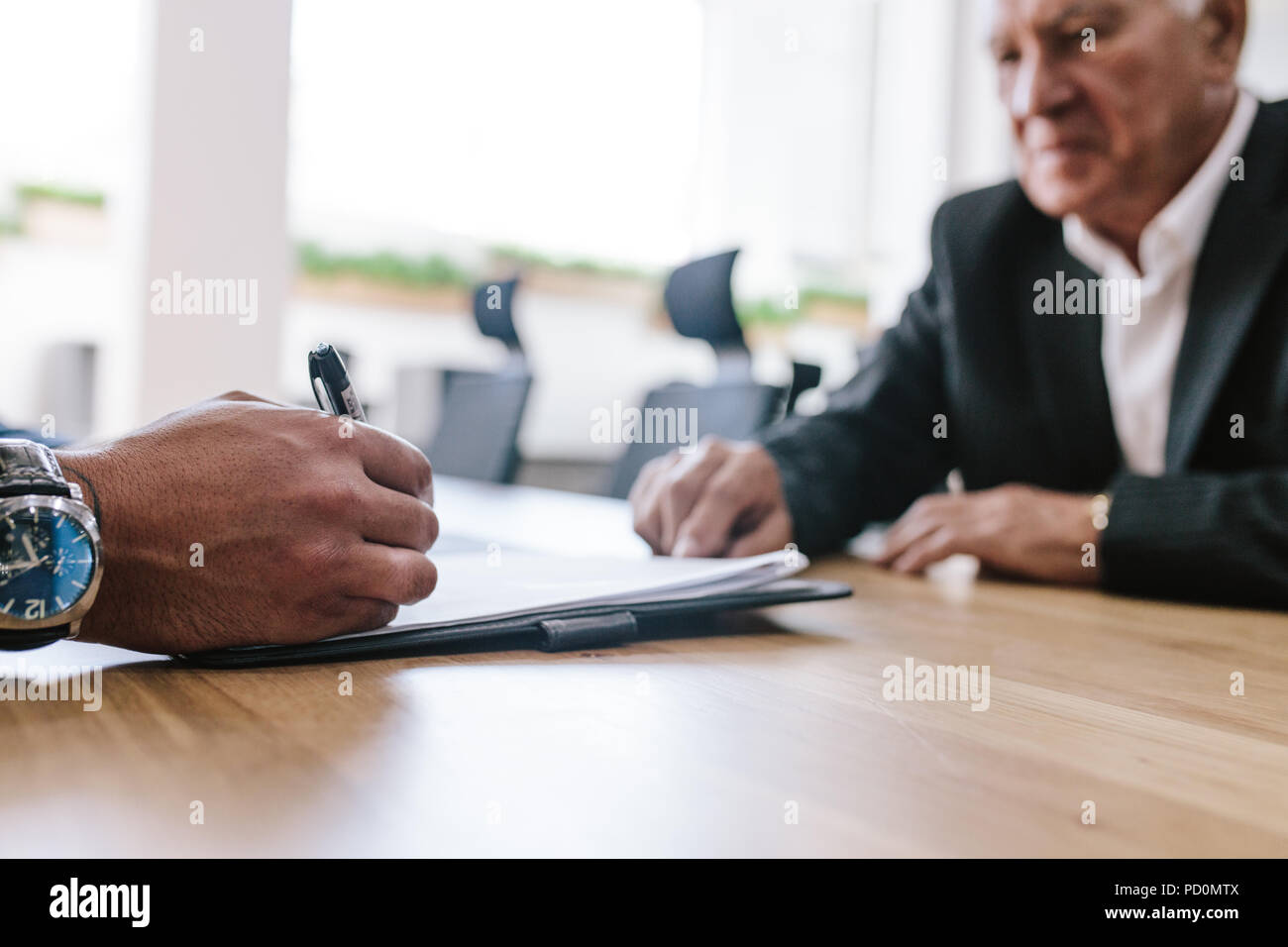 Hand of young man signing contract with senior man sitting around the ...