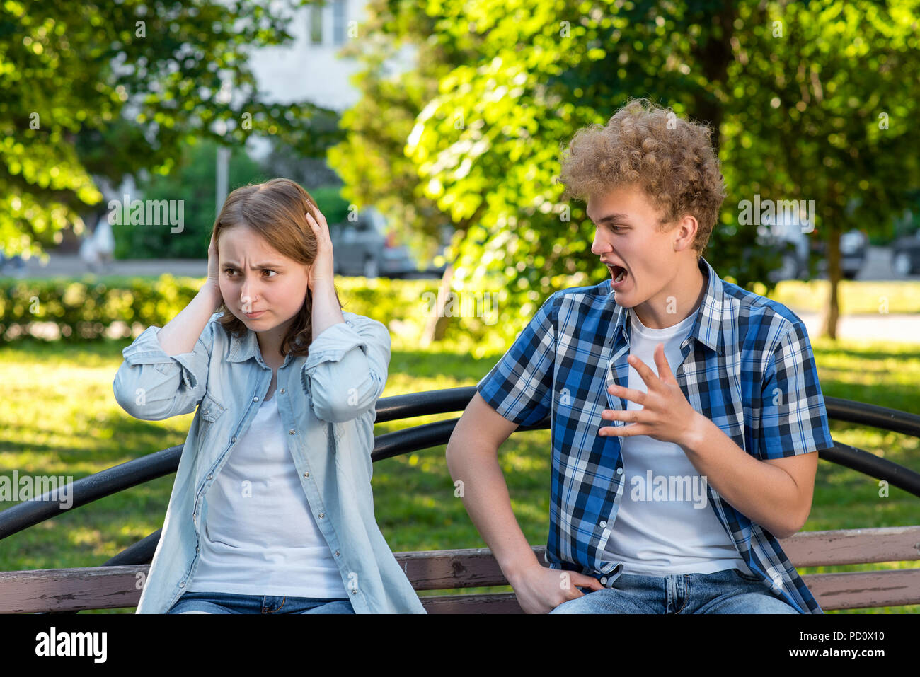 A young guy screams at a girl. Summer in park on a bench. The girl ...