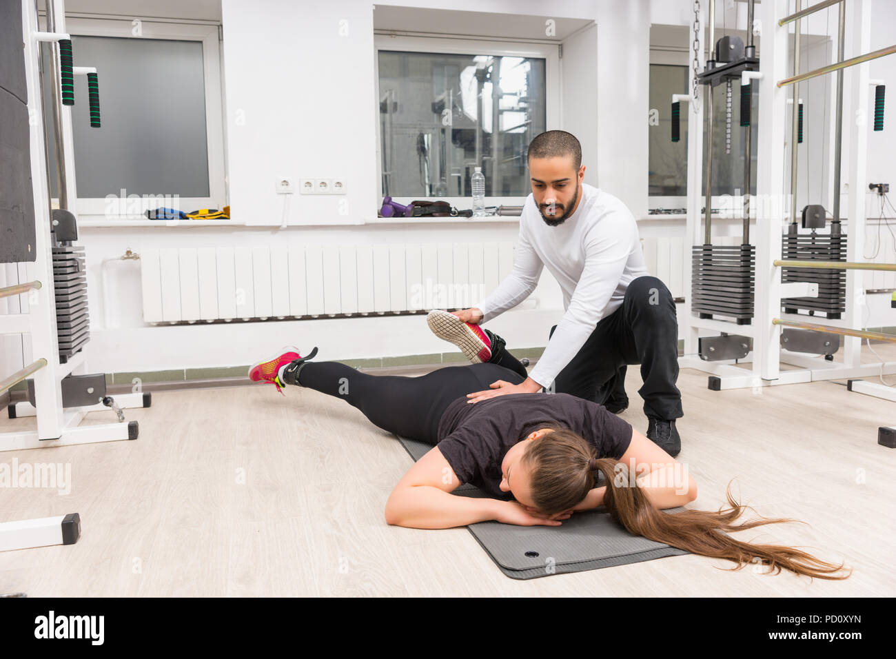 Personal trainer assisting a woman with her workout in a gym bending ...