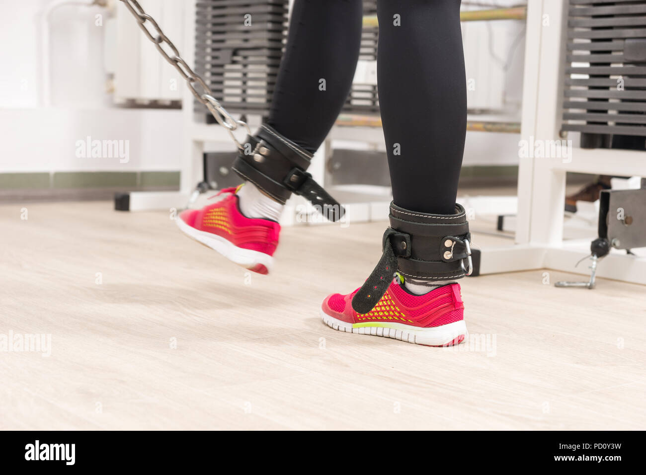 Woman wearing leather ankle straps attached to a chain in a gym while ...