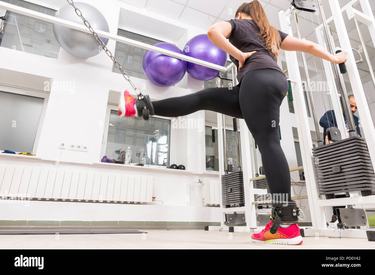 Rear view of woman exercising legs with weight on cable crossover ...