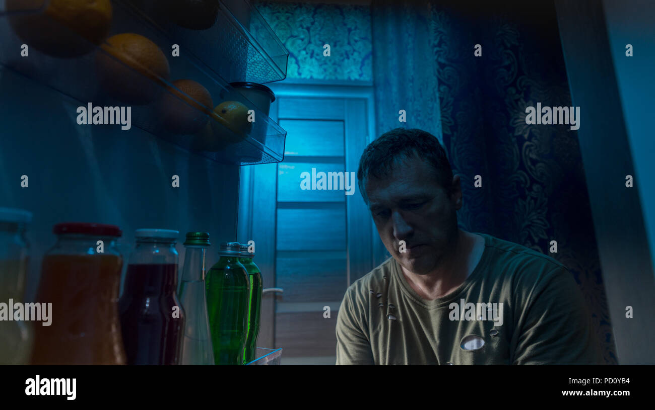 Man searching in his fridge in the darkness for something to snack on ...