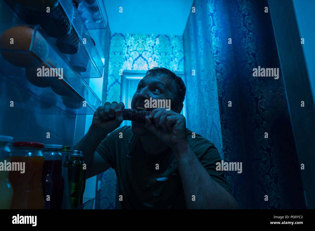 Man snacking on a whole spicy salami from the fridge in the night ...