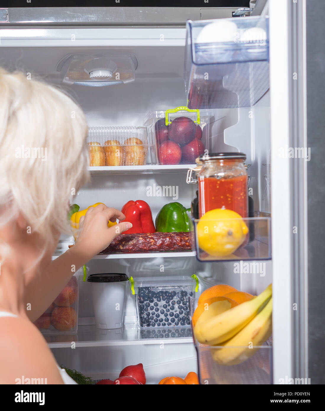 Rear view of woman reaching for food in open fridge Stock Photo - Alamy