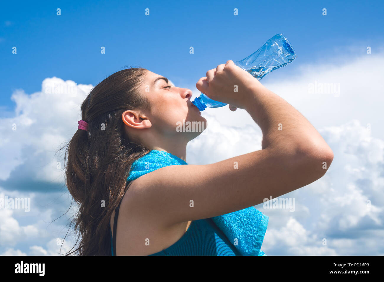 Beautifull girl runner is having break, drinking water against clear ...