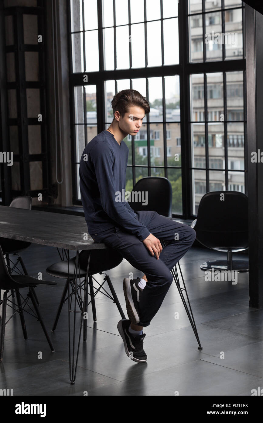Dreamy handsome slim young guy sitting on a table with his head down ...