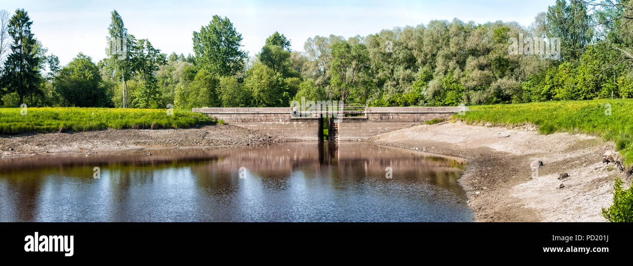 A concrete pedestrian bridge in a park on a shallow river shows sloping ...