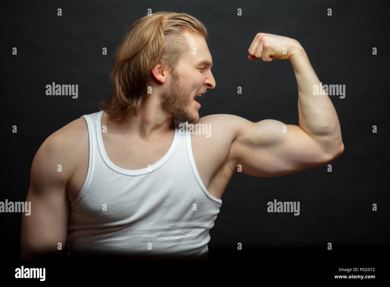joyful athlete admiring with his strong arms isolated on the black ...