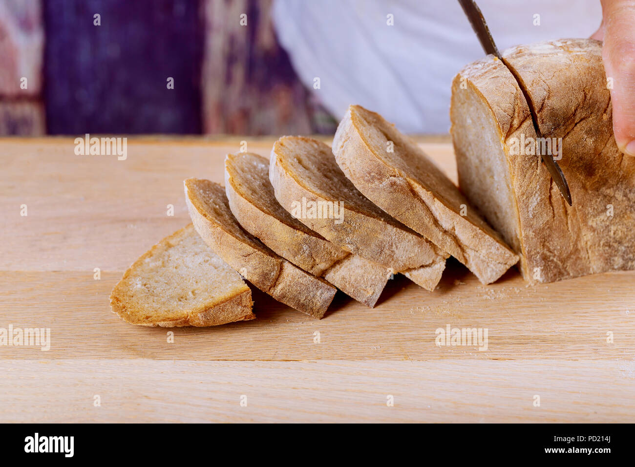 Fresh whole grain bread on kitchen table or wooden bread board with man ...