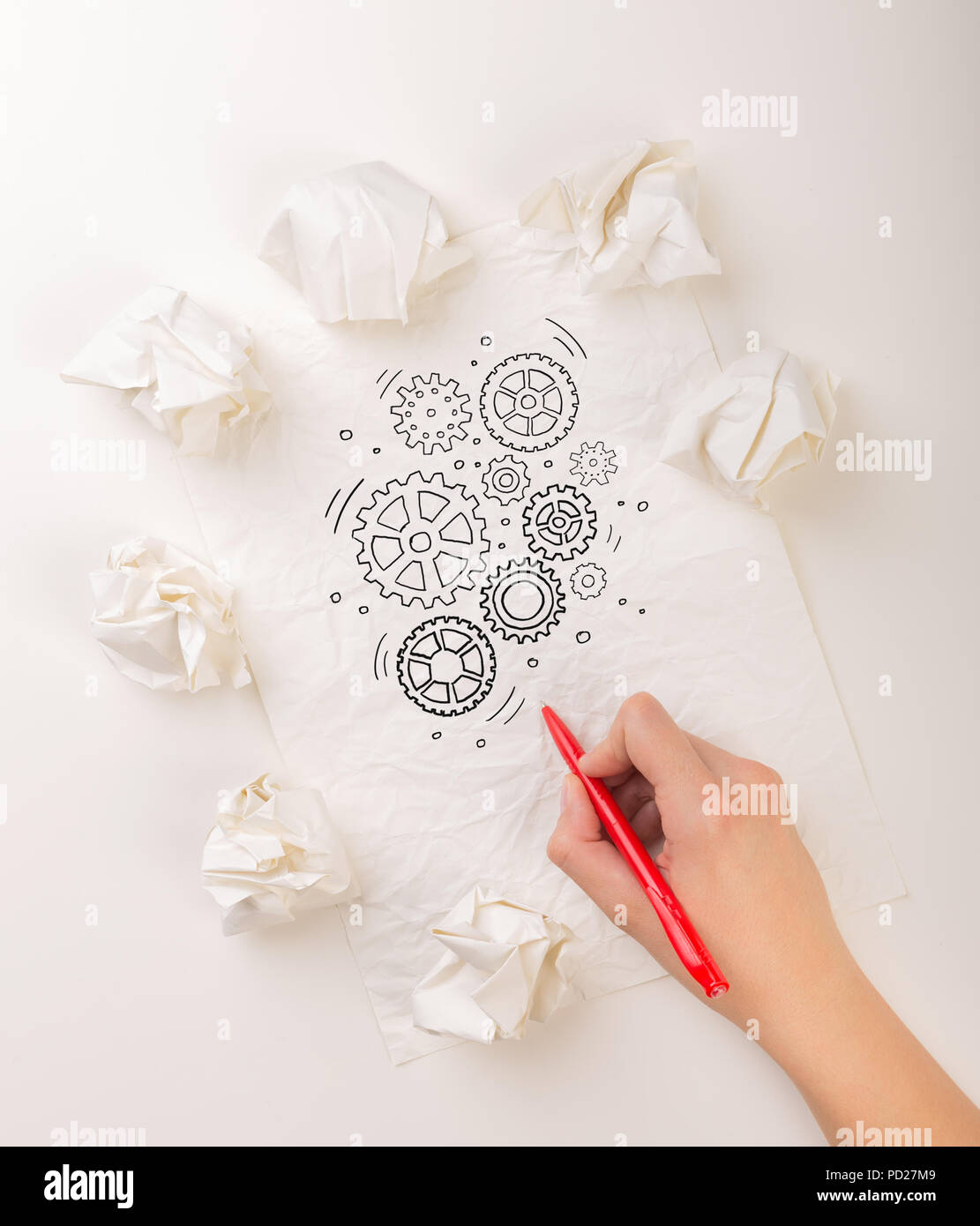 Female hand next to a few crumpled paper balls drawing rotating gears ...