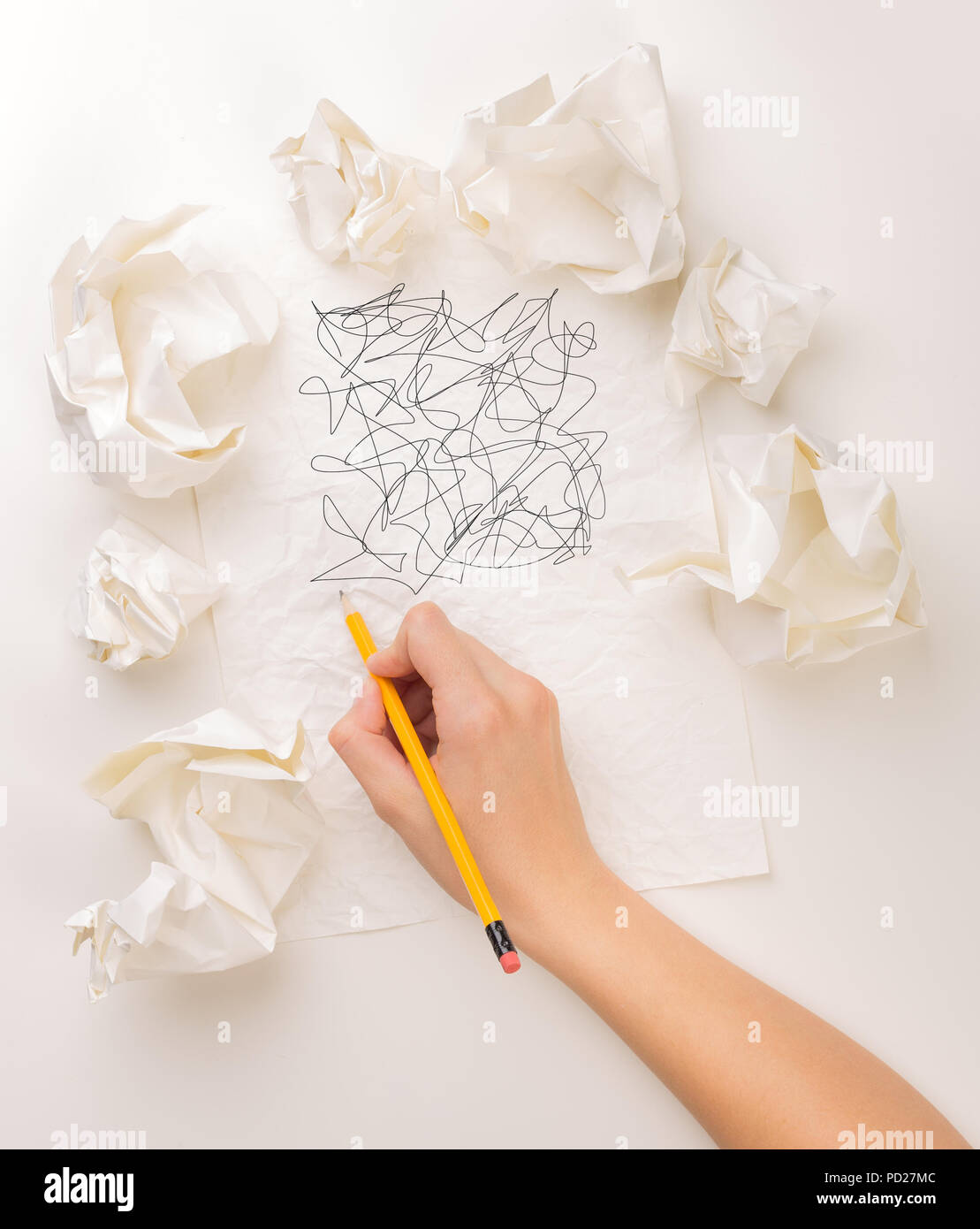 Female hand next to a few crumpled paper balls drawing random scribbles ...