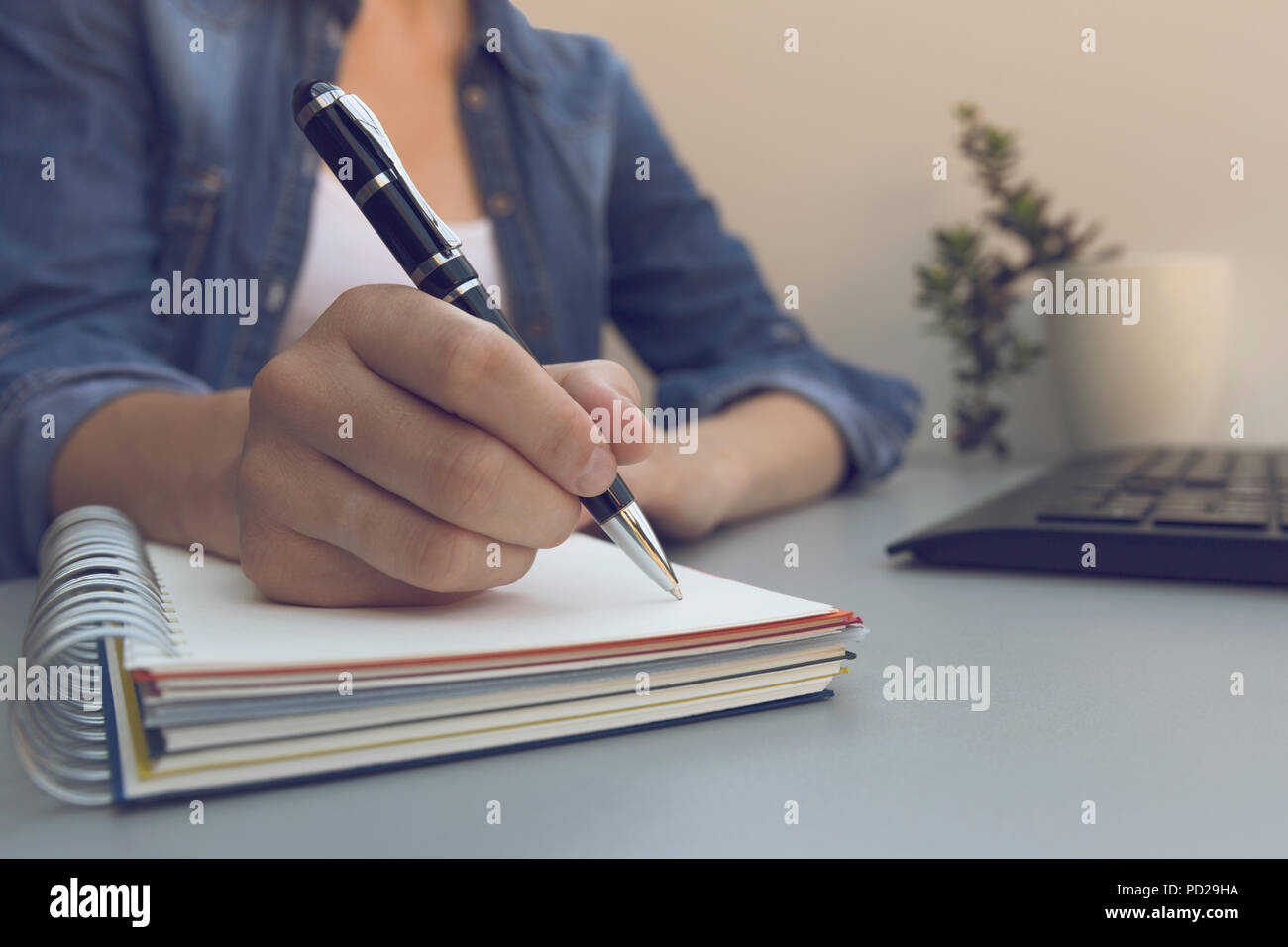 Woman's hands with pen writing on notebook. Modern grey office desk ...