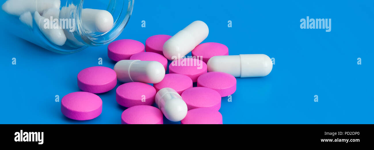 Large and bright red and white pills are scattered from a glass jar. On ...