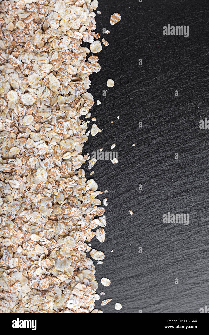 raw oatmeal is scattered on a black background, on slate blackboard ...