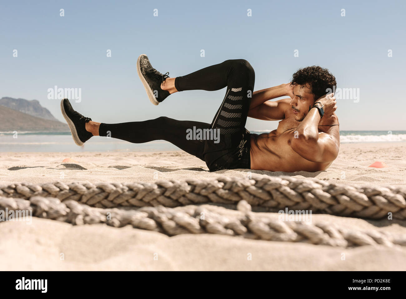 Bare chested man doing abdomen exercise at a beach with a battle rope ...
