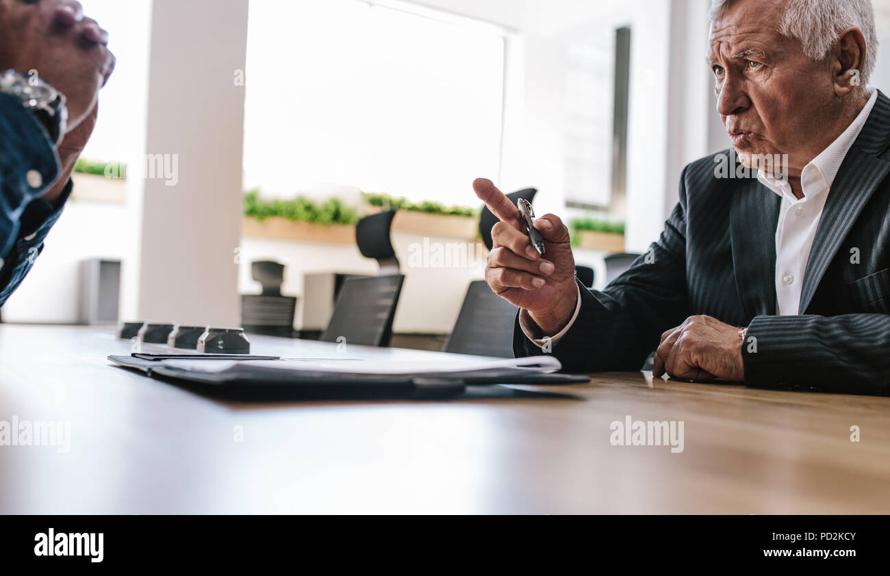 Senior businessman talking with male colleague sitting around a table ...