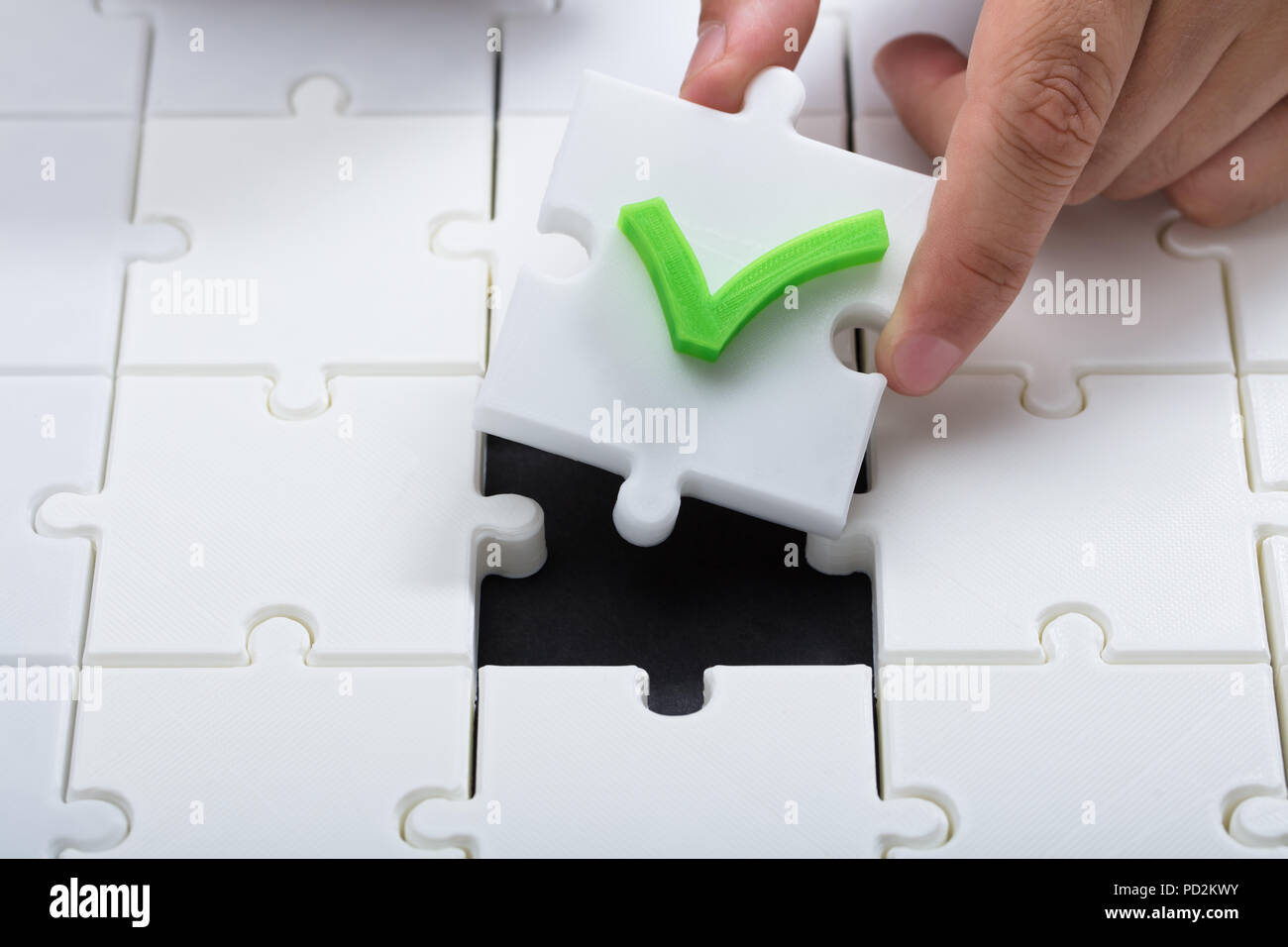 Human hand solving jigsaw puzzle by connecting white piece with check ...