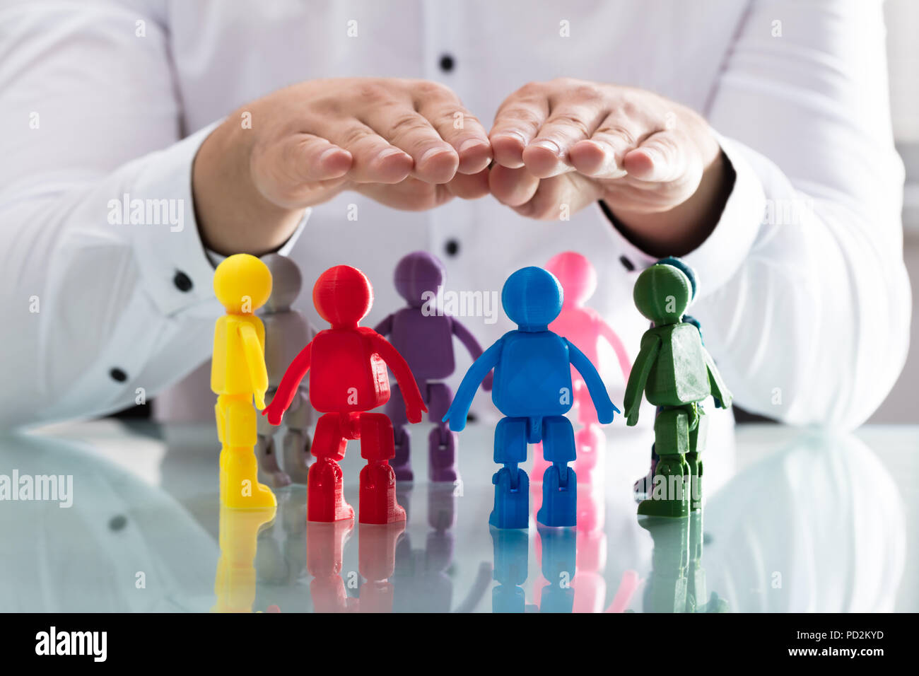 A person's hand protecting multi colored human figures forming circle ...