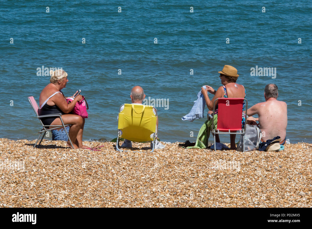 four older retired people sunbathing sitting in chairs on the beach ...
