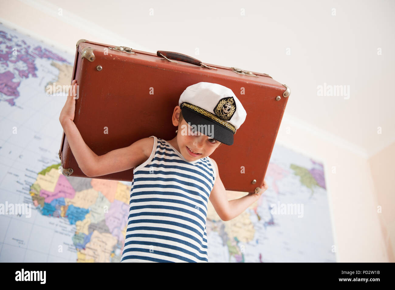 strong kid in captain cap holding heavy suitcase on his back on world ...