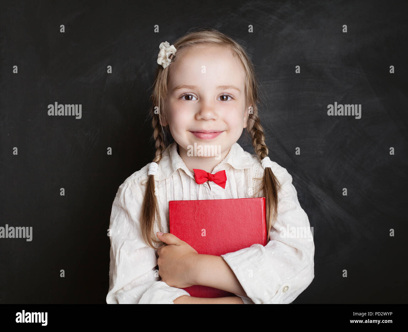 Cute child girl with book having fun on chalkboard background in ...