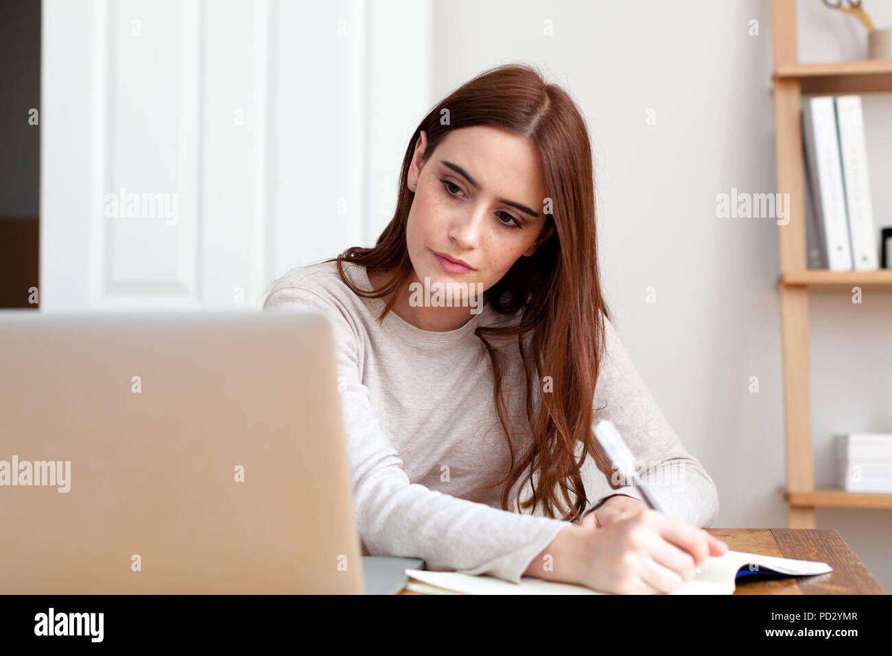 Woman writing notes into notepad from laptop Stock Photo - Alamy