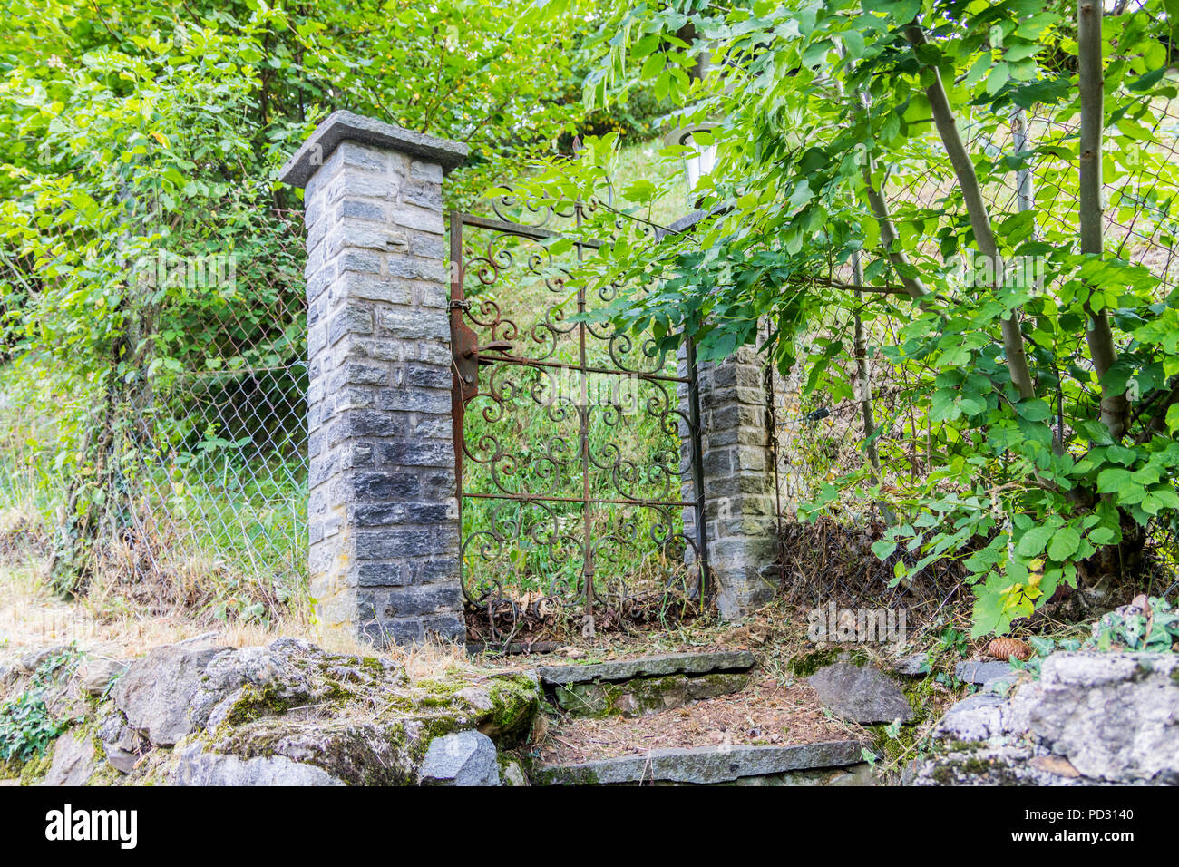 Old vintage rusty ornate gates between stone walls in a forest setting ...