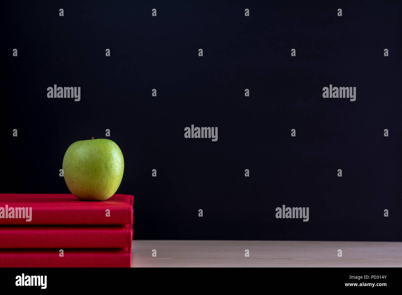 School supplies and apple on classroom table in front of blackboard ...