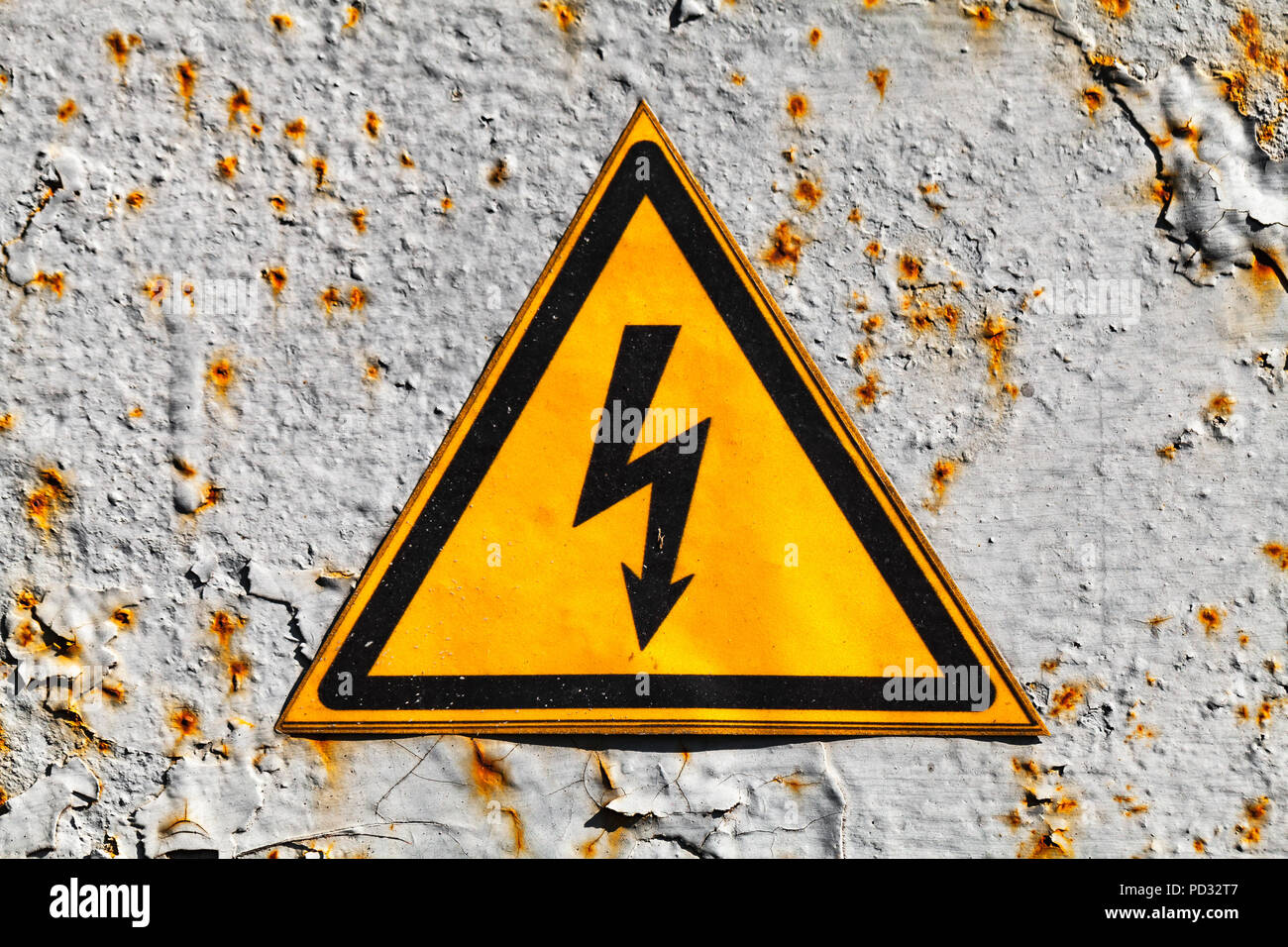 Yellow high voltage triangle warning sign on rusty gray metal wall ...