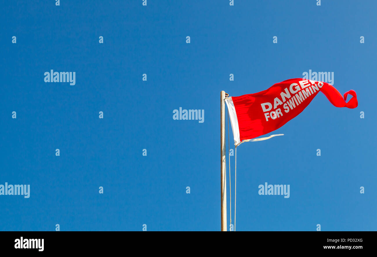 Danger for swimming. Red warning flag on a beach waving above blue sky ...