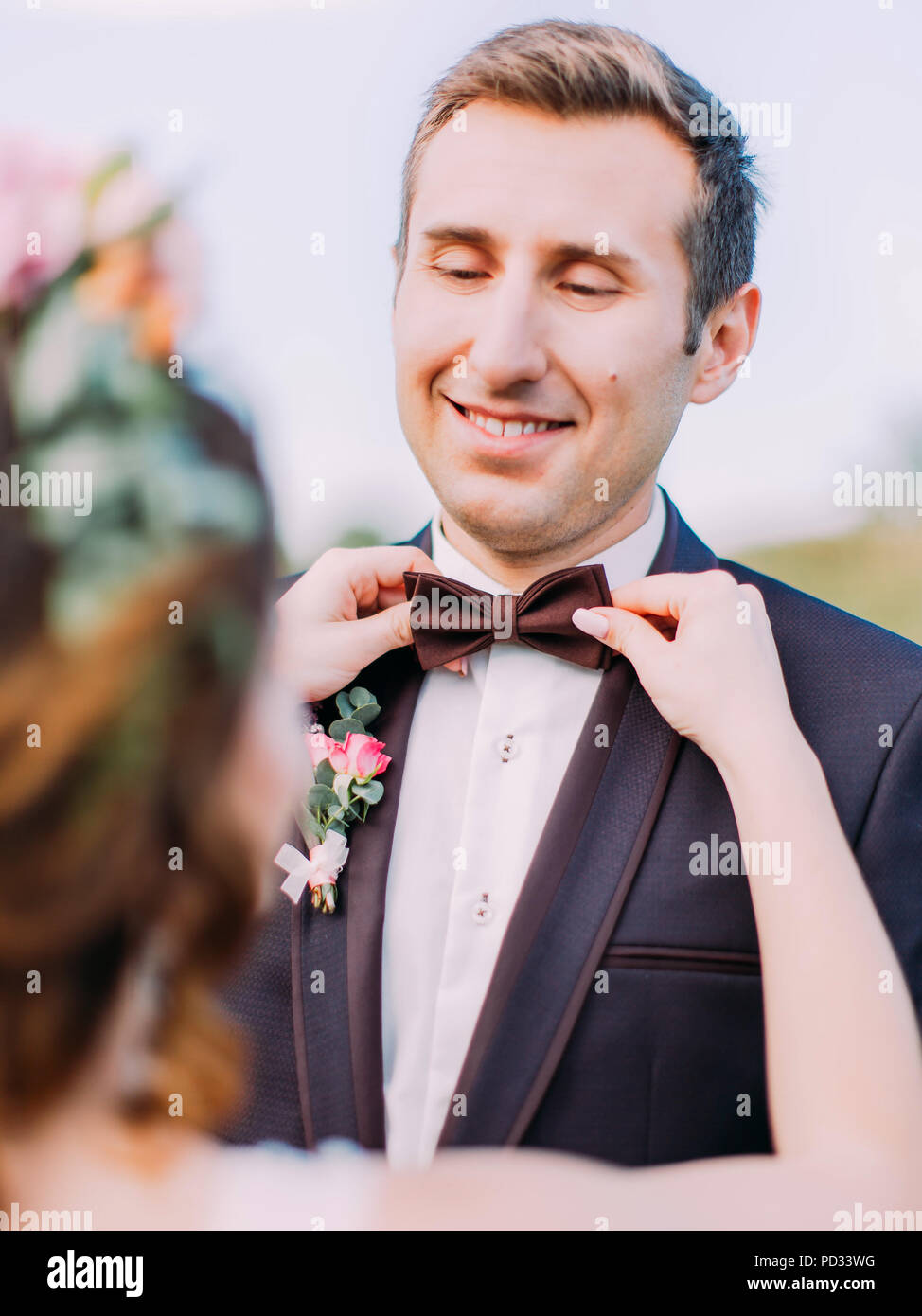 The close-up view of the smiling groom. The bride is correcting the bow ...