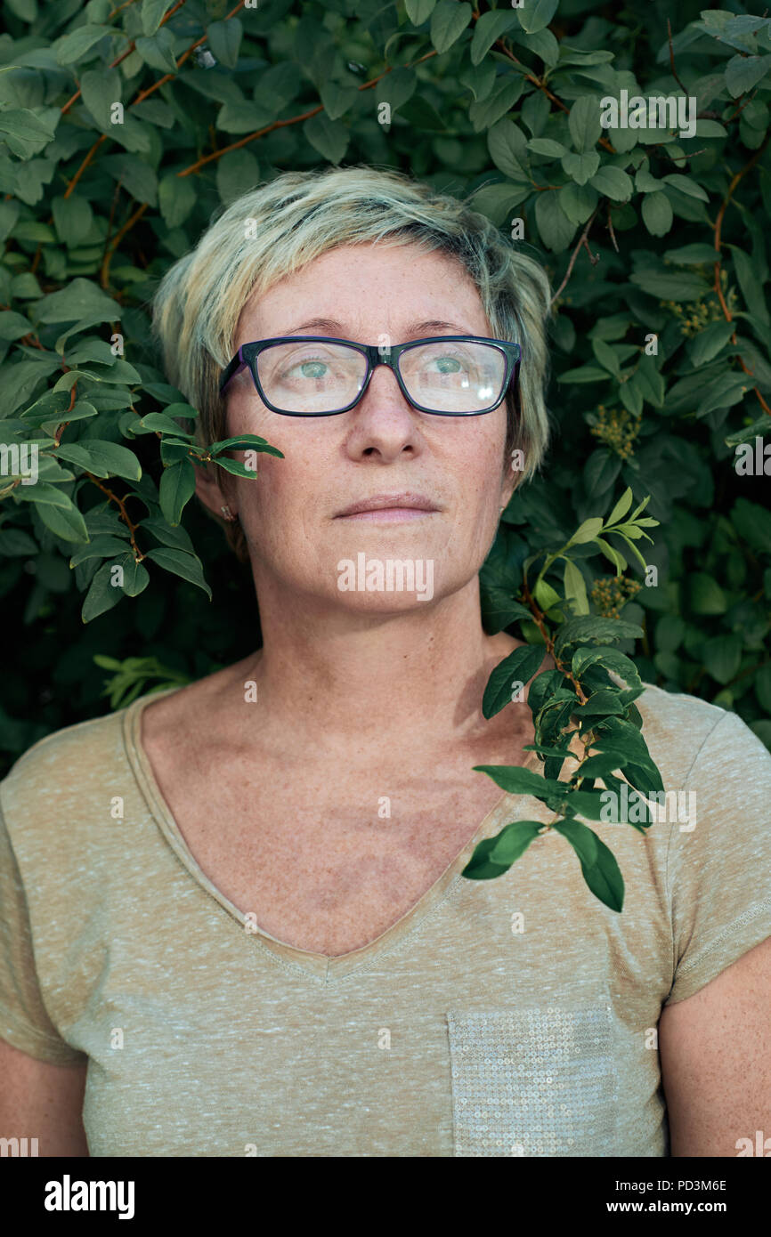 Aged lady near bush looking away Stock Photo - Alamy