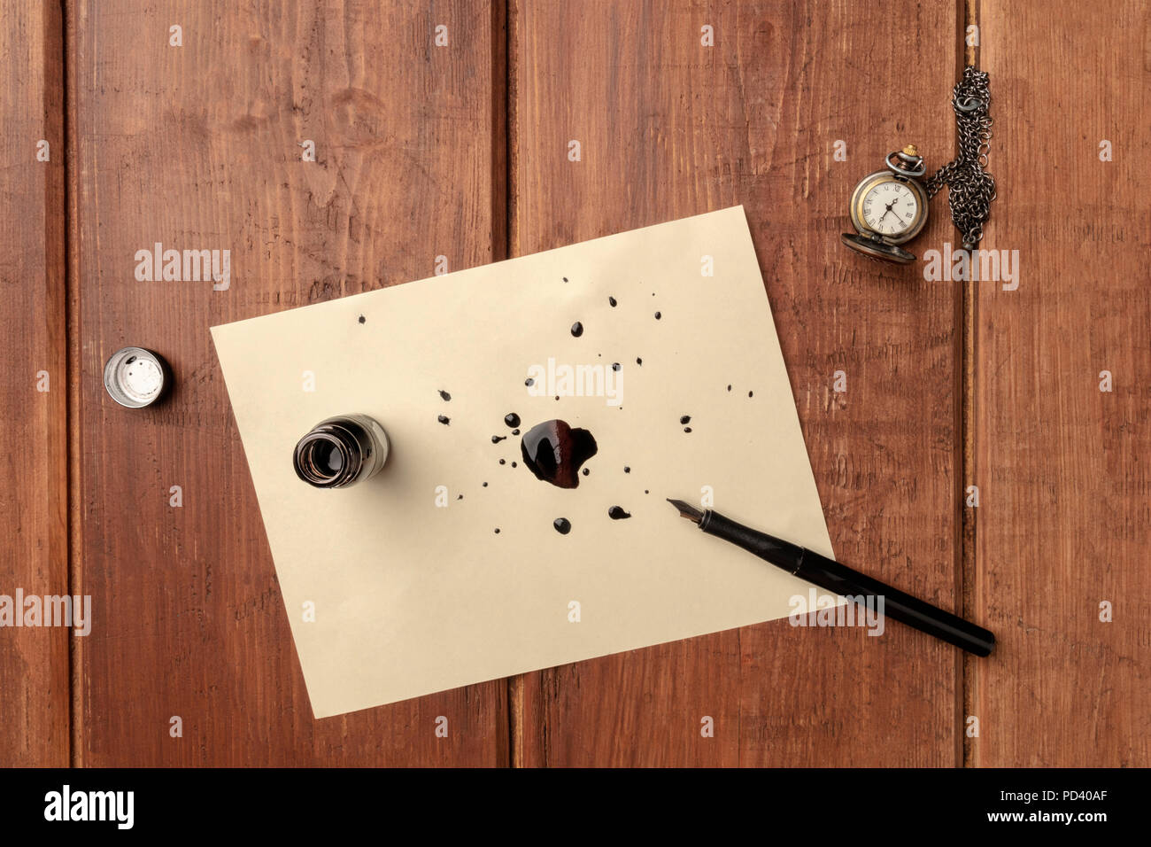 An overhead photo of an ink well with drops of ink and a nib pen, with ...