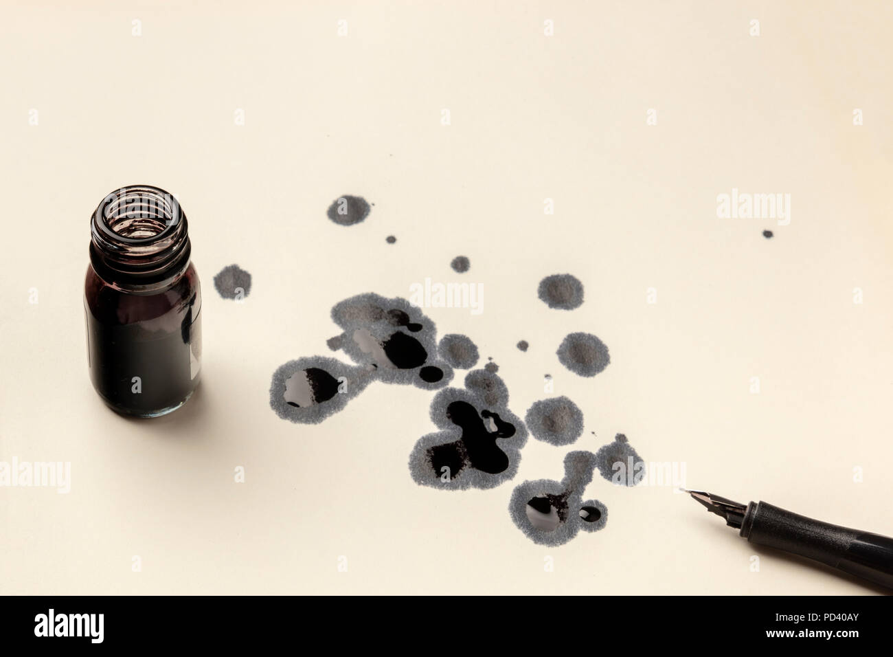 A photo of an ink well with drops of ink on a textured off-white paper ...