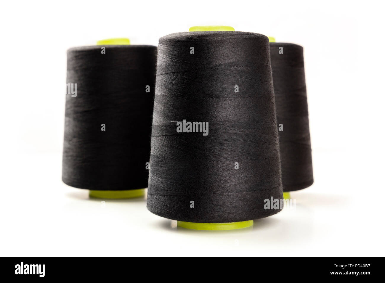 A side view of three large black thread spools on a white background ...