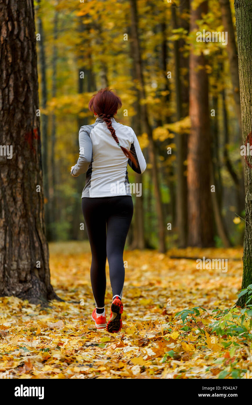 Picture from back of young sporty brunette in running through forest ...
