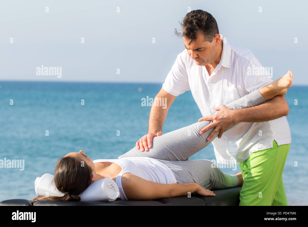 Close up of male osteopath doing hip and leg treatment outdoors on ...