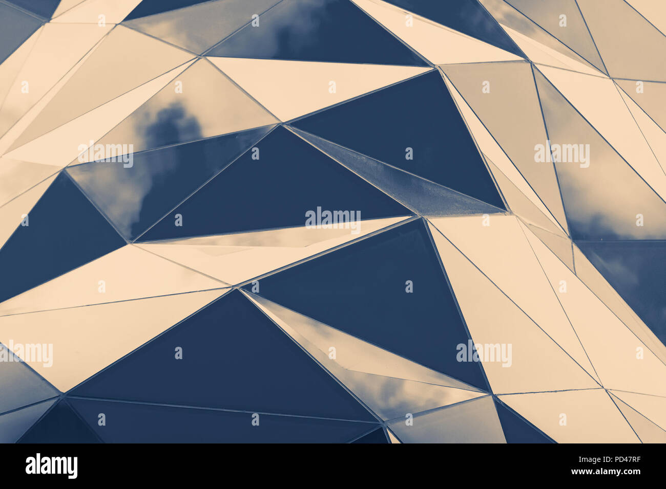 Polygonal triangle glass facade of modern building. Cloudy sky reflects ...